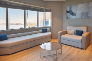 Uma sala de estar moderna com uma janela grande, um sofá, uma poltrona e uma mesa de centro de vidro.