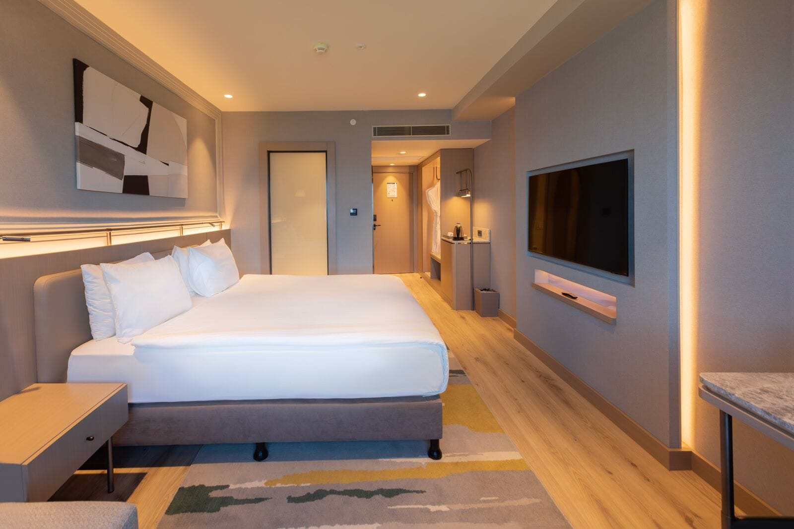 Quarto de hotel moderno com uma cama grande, TV fixada na parede e uma pequena mesa.
