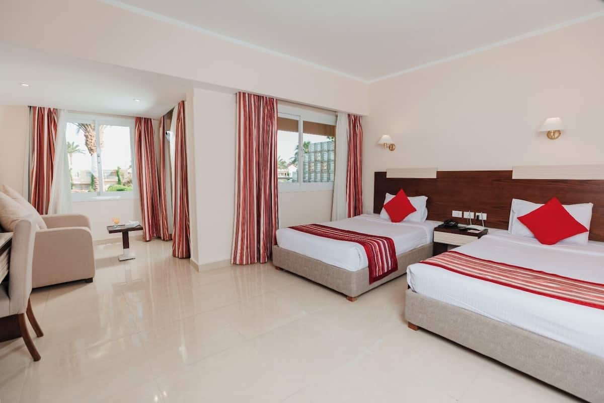 Quarto de hotel com duas camas, um sofá, uma mesa pequena e uma janela com cortinas.