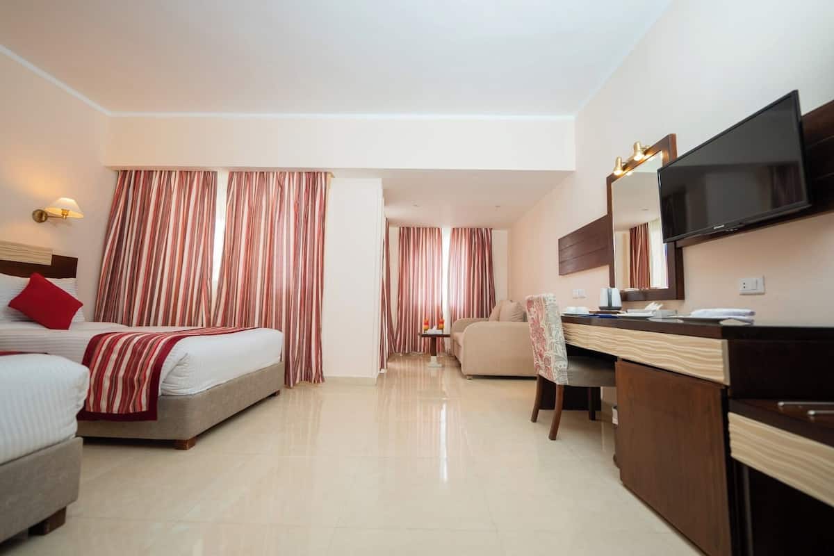 Quarto de hotel com cama, escrivaninha, cadeira, televisão e cortinas.