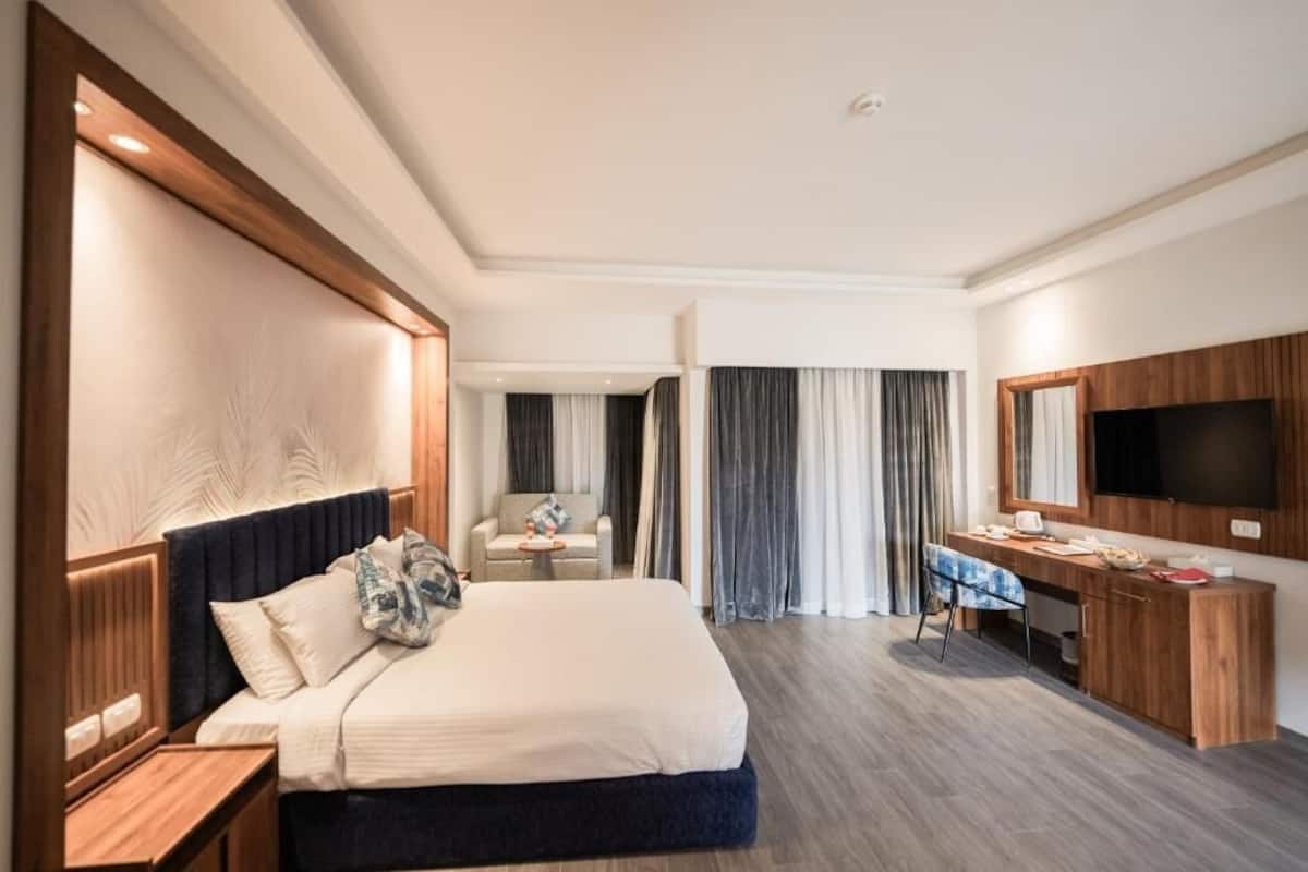 Quarto de hotel com uma cama grande, uma escrivaninha, uma cadeira, uma televisão e uma pequena mesa.