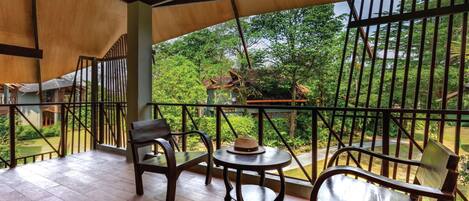 Um deck de madeira com mesa e cadeiras, com vista para um jardim exuberante e um edifício com telhado inclinado.