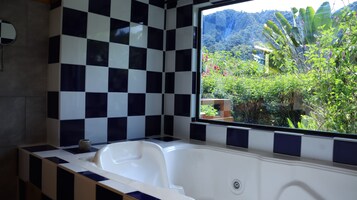 Casa de banho com parede de azulejos preto e branco carinhosamente estampada, uma banheira branca e uma janela com vista para um jardim exuberante.