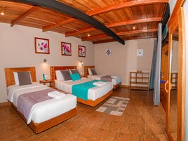 Quarto de hotel com três camas, piso de madeira e teto com vigas aparentes.