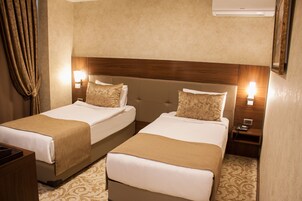 Quarto de hotel com duas camas, uma cabeceira de madeira, luminárias de cabeceira, telefone e ar condicionado.