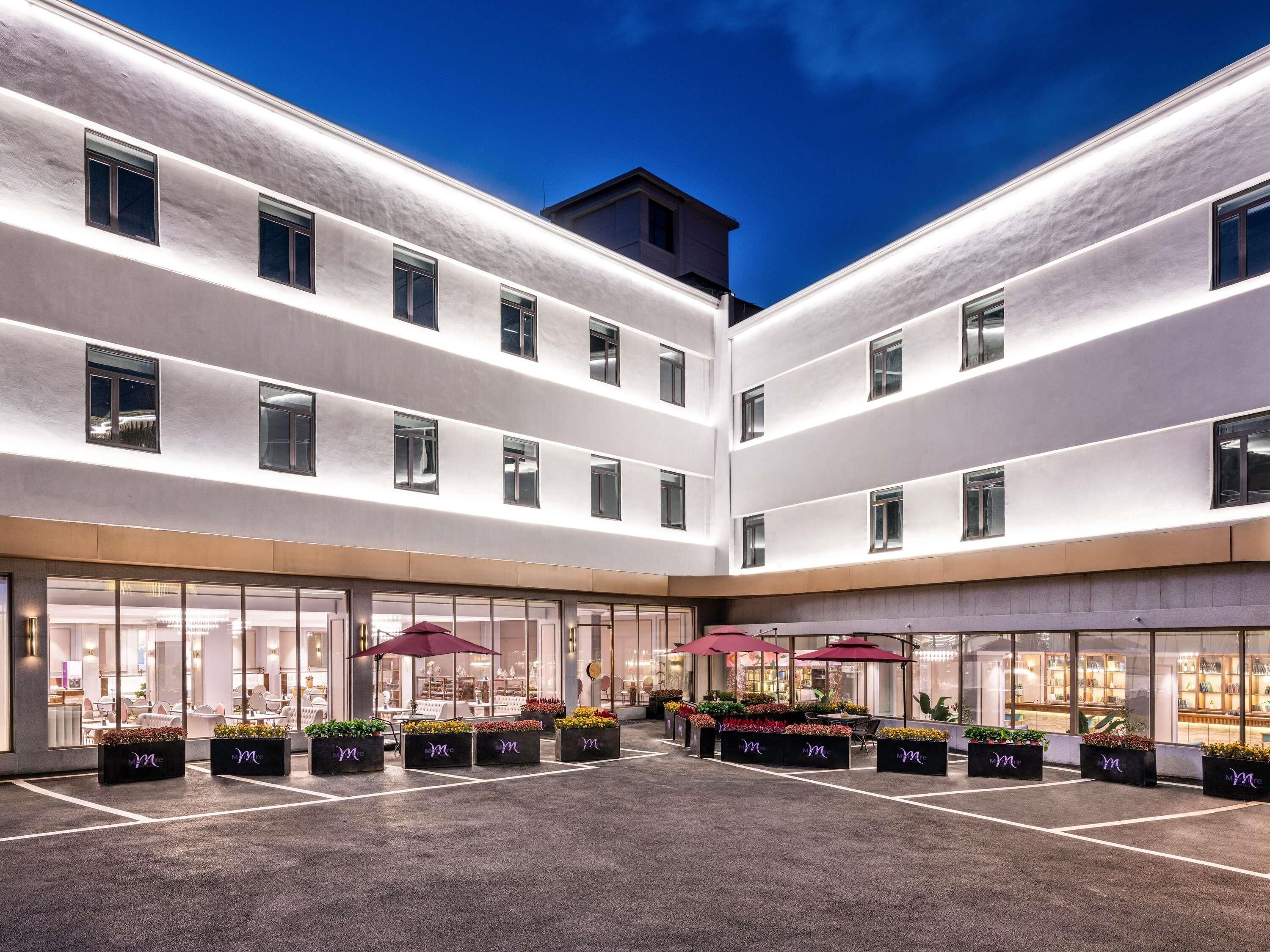 Pátio de hotel com vários andares, janelas amplas e áreas de estar ao ar livre com guarda-sóis.