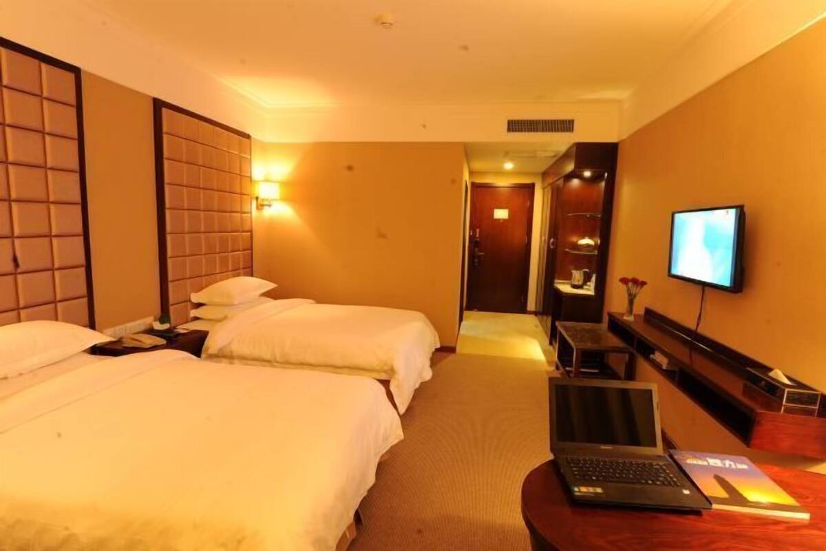 Quarto de hotel com duas camas, uma mesa de escritório com um laptop, uma televisão e uma pequena mesa com um vaso.