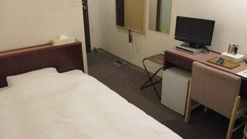 Quarto de hotel com cama, escrivaninha com computador, cadeira e um pequeno frigorífico.