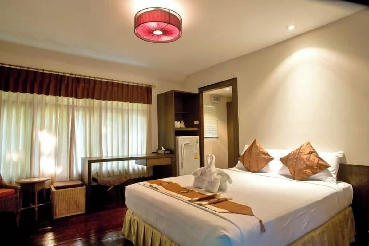 Quarto de hotel com cama, escrivaninha, cadeira, espelho e janela com cortinas.