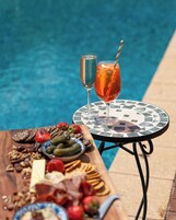 Mesa à beira da piscina com chá gelado, champanhe e um prato de petiscos.
