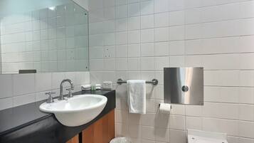 Uma casa de banho moderna com lavatório branco, bancada preta, espelho, azulejos brancos e sanita.