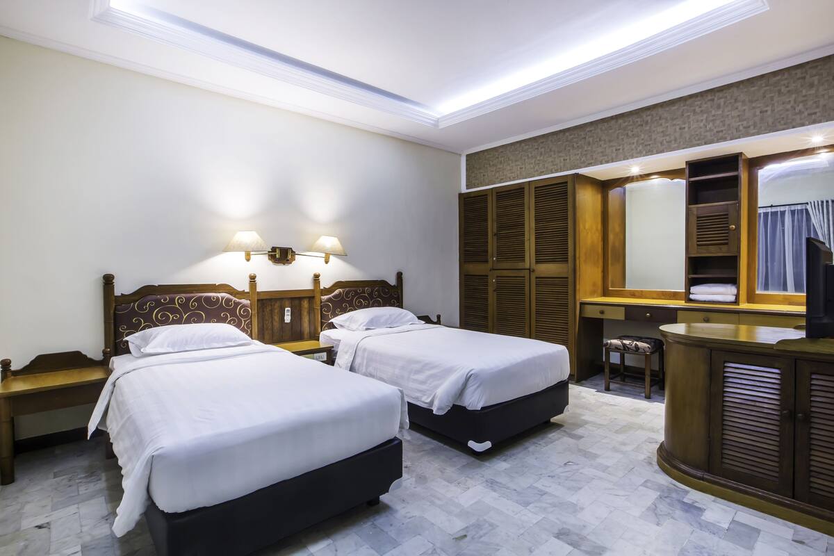 Quarto de hotel com duas camas, uma escrivaninha, uma cadeira, toucador com espelho e armários embutidos.
