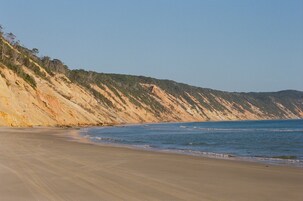 Uma praia com areal e um penhasco íngreme com vegetação esparsa.