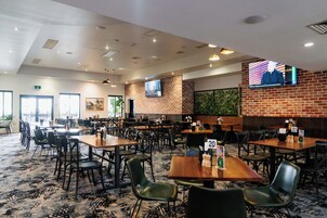 Uma sala de jantar ampla com várias mesas e cadeiras, uma parede de tijolos e uma televisão fixada na parede.