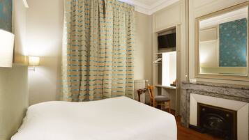 Quarto de hotel com uma cama grande, lareira, uma cadeira e janela com cortinas.
