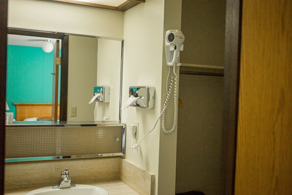 Casa de banho com lavatório, espelho e secador de cabelo fixado na parede.