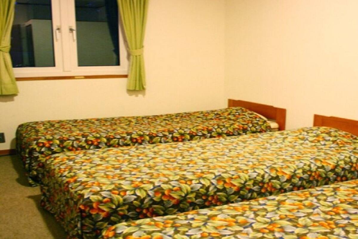 Quarto com duas camas, uma janela com cortinas e uma parede lisa.