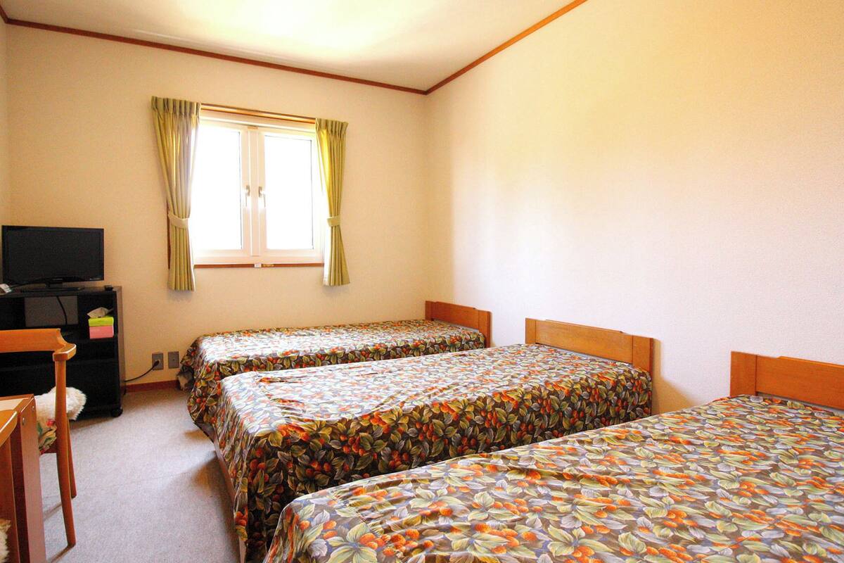 Quarto com duas camas, uma escrivaninha com televisão e uma janela com cortinas.