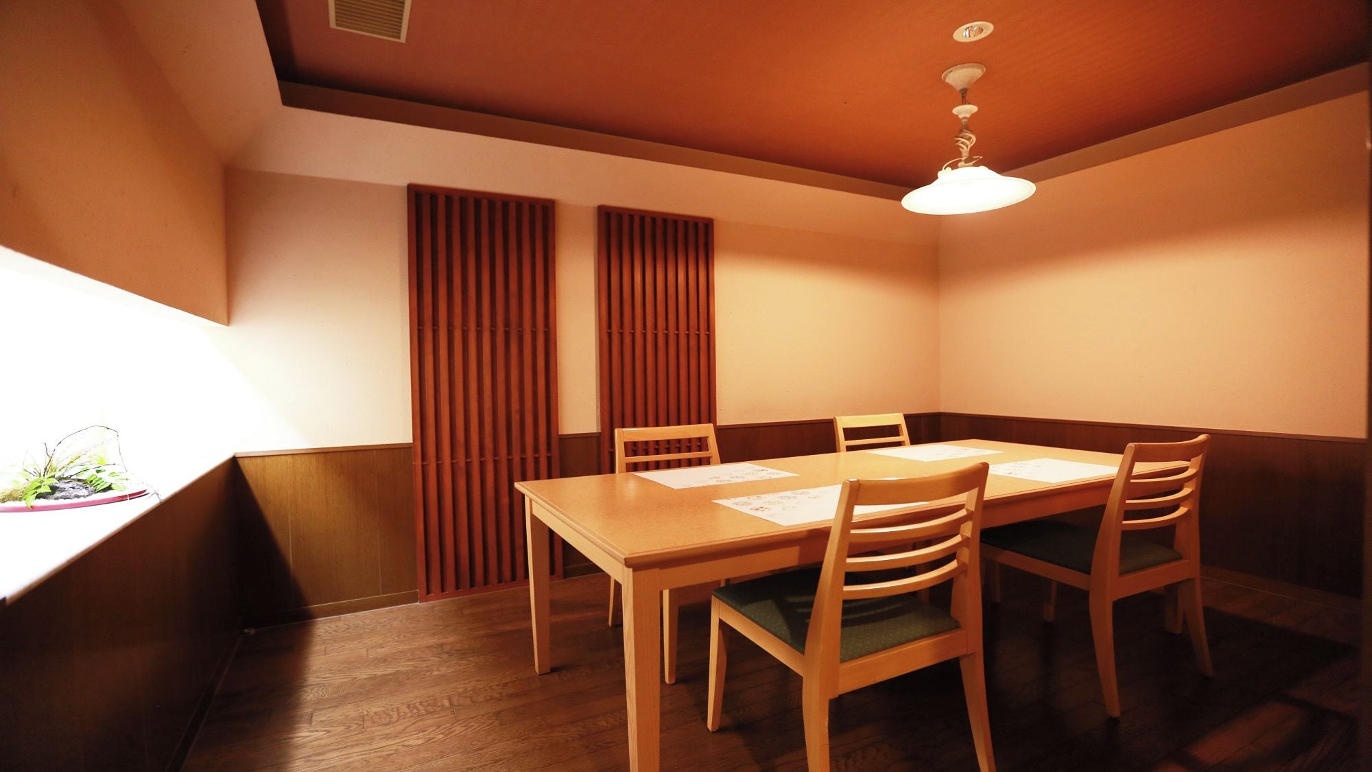 Uma sala de conferências com mesa e cadeiras de madeira, um ventilador de teto e uma janela com persianas.