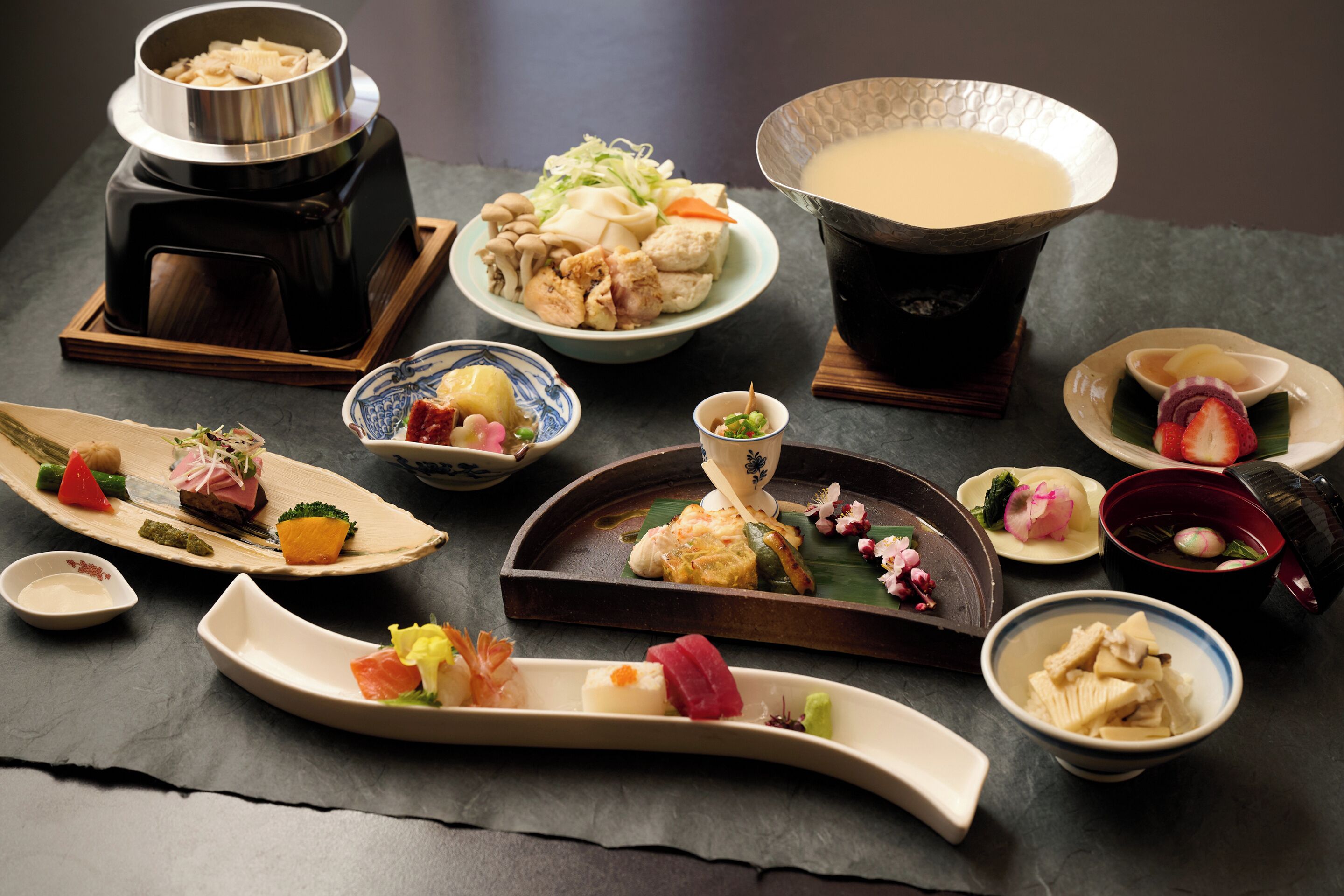 Diversos pratos japoneses dispostos numa mesa, incluindo sushi, tempura e um pote quente.