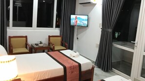 Quarto de hotel com cama, duas cadeiras, uma mesa pequena, televisão e janela com cortinas.