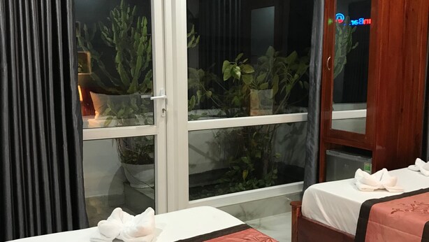 Quarto de hotel com duas camas, porta de correr de vidro para uma varanda com plantas e um armário de madeira.