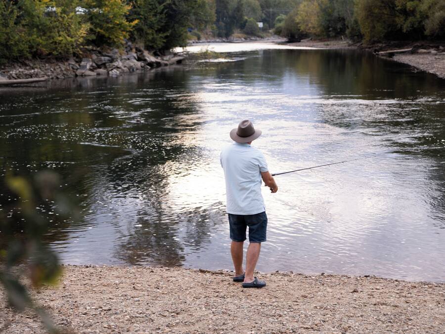 Um homem pesca em um rio, com árvores e um céu limpo ao fundo.