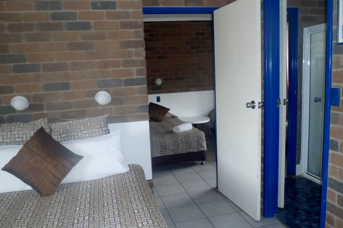 Quarto de hotel com parede de tijolos, cama com roupa de cama estampada, mesa de cabeceira e banheiro com porta de vidro.