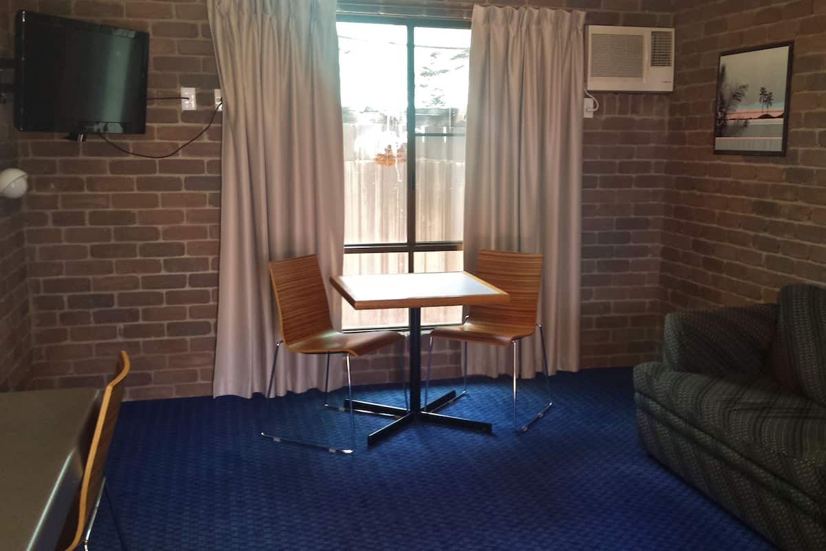 Quarto com parede de tijolos, televisão na parede, mesa com duas cadeiras, sofá e janela com cortinas.