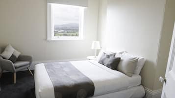 Quarto com cama, uma cadeira, mesa de cabeceira, luminária e janela com vista para a paisagem.