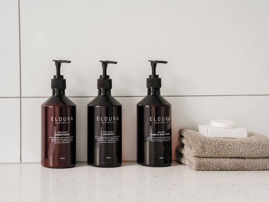 Três frascos de produtos de cuidados para a pele Eloura Australia e uma toalha dobrada em uma bancada de banheiro.