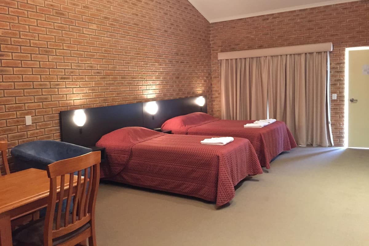 Quarto com duas camas, uma escrivaninha de madeira e uma cadeira.