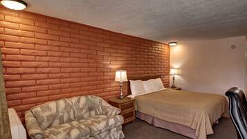 Quarto de hotel com parede em padrão de tijolos, cama com colcha bege, poltrona estampada e duas luminárias de cabeceira.