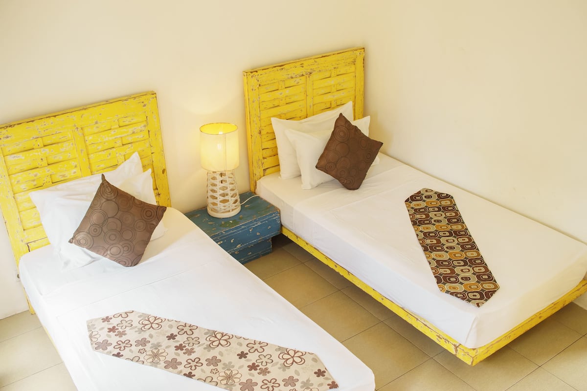 Duas camas de solteiro com cabeceiras amarelas, roupa de cama branca e almofadas decorativas.
