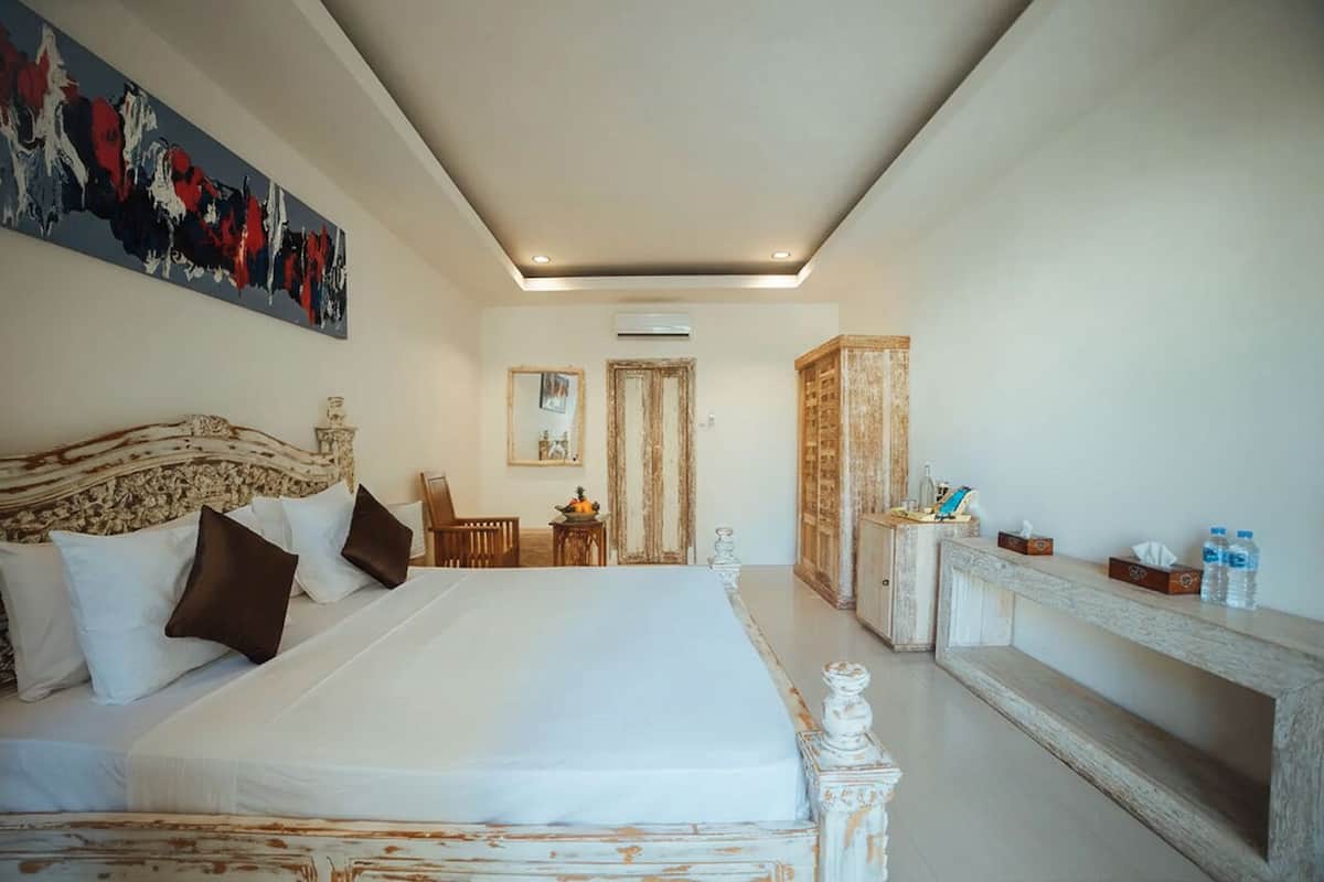Um quarto espaçoso com uma cama grande, cabeceira de madeira, uma mesa pequena com uma cadeira e um banquinho com espelho.