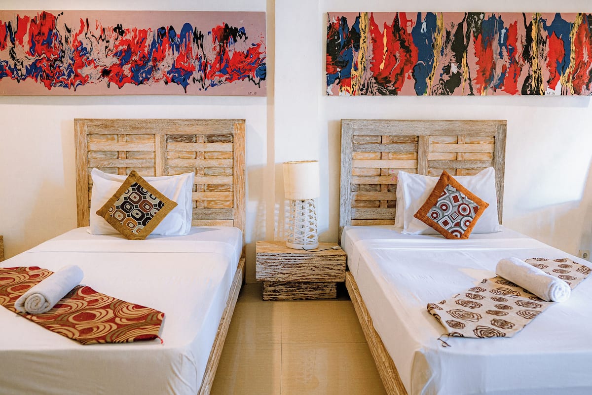 Duas camas de casal com cabeceiras de madeira, roupa de cama branca, almofadas estampadas e toalhas enroladas.