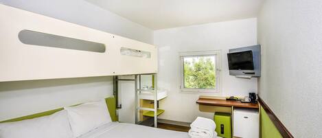 Quarto de hotel com cama beliche, uma escrivaninha com televisão, janela e uma pequena cozinha equipada.