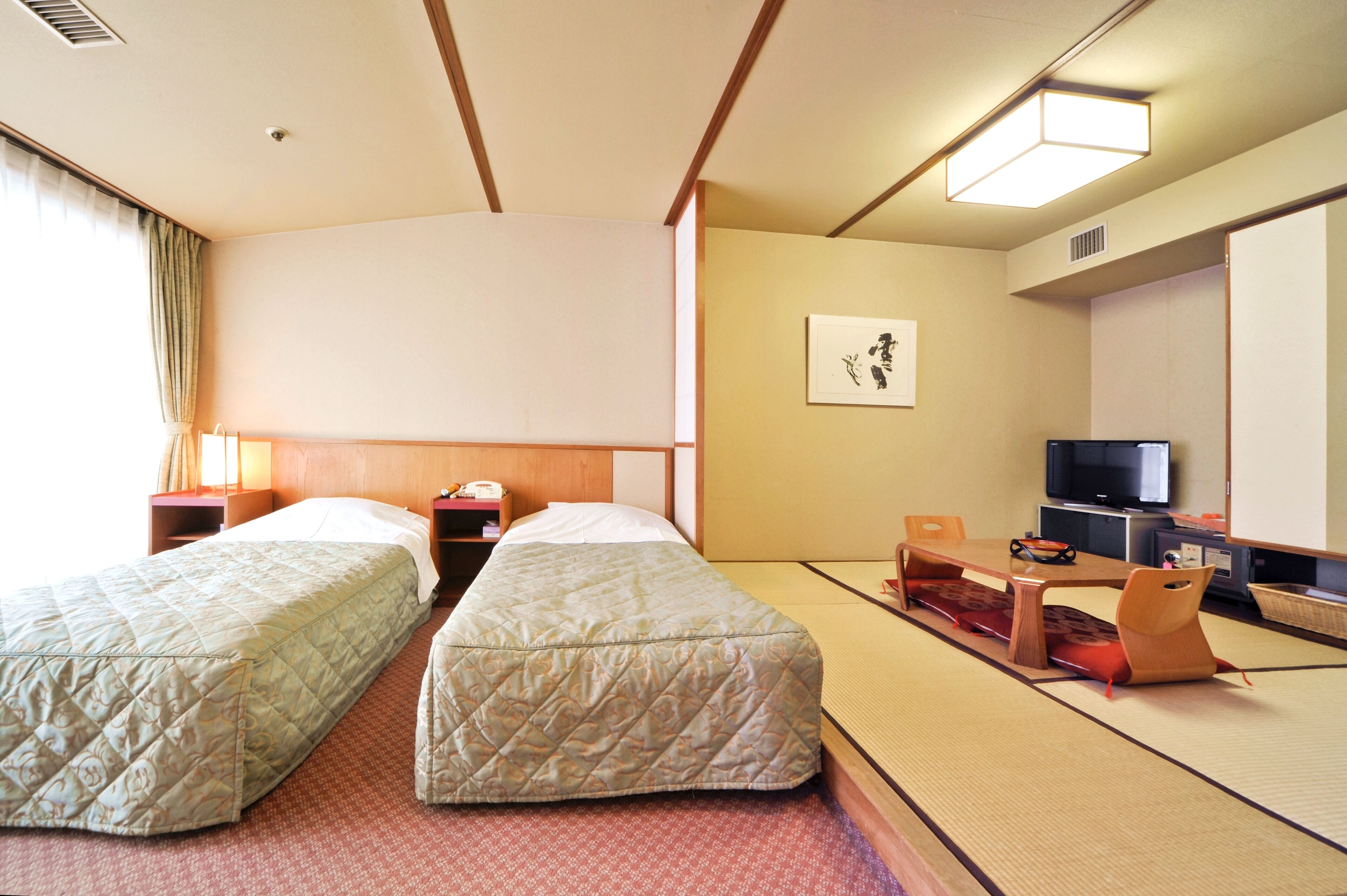 Quarto de hotel com duas camas, televisão, uma mesinha e piso tradicional de tatame japonês.