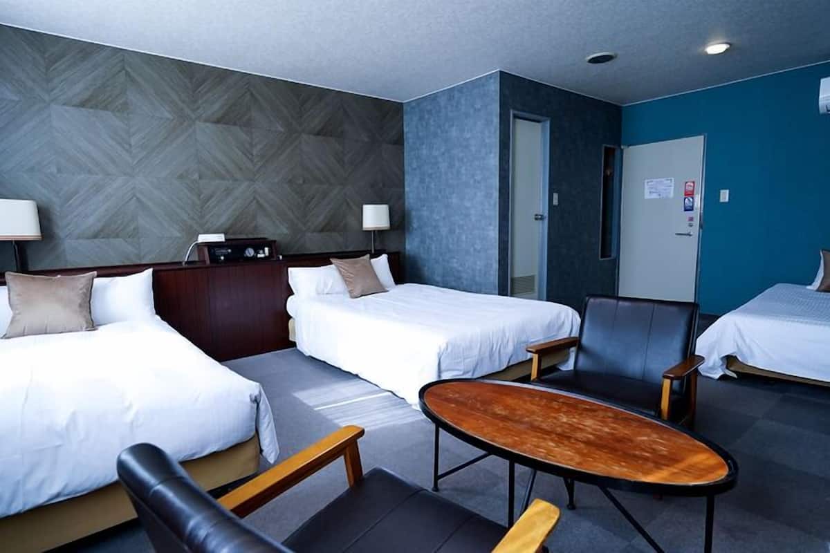 Quarto de hotel com duas camas, uma escrivaninha, uma cadeira e uma mesinha.