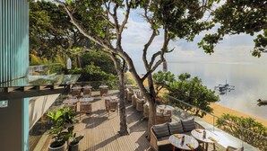 Terraço com mobiliário de vime, guarda-corpo de vidro e vista para o mar.