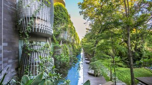 Uma trilha estreita ladeada por vegetação exuberante e um edifício com jardins verticais.