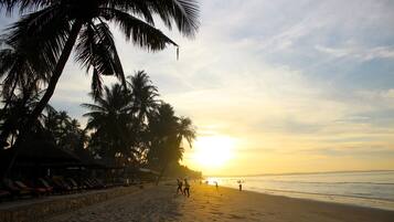Uma praia com palmeiras, espreguiçadeiras e um pôr do sol.