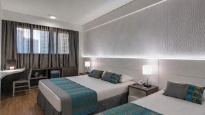 Quarto de hotel com duas camas, uma escrivaninha e uma cadeira.
