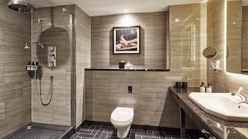 Uma casa de banho moderna com duche, sanita e lavatório, com chão em mosaico e um quadro emoldurado na parede.