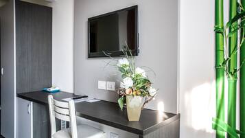 Uma cozinha moderna com bancada escura, uma cadeira branca, um vaso com flores e uma televisão na parede.