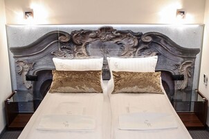 Cama de casal com cabeceira ornamentada, duas almofadas e mesas de cabeceira.