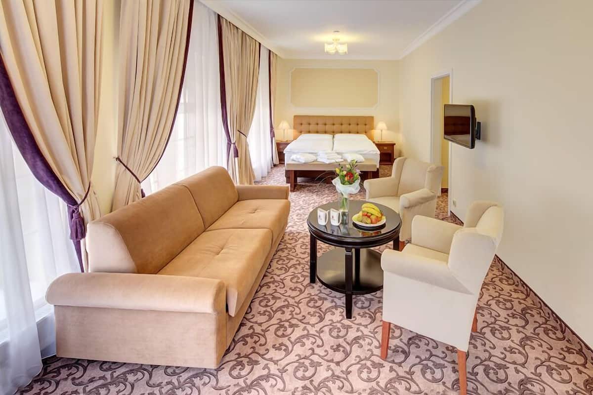 Quarto de hotel com sofá, poltronas, cama, televisão e uma mesinha com frutas.