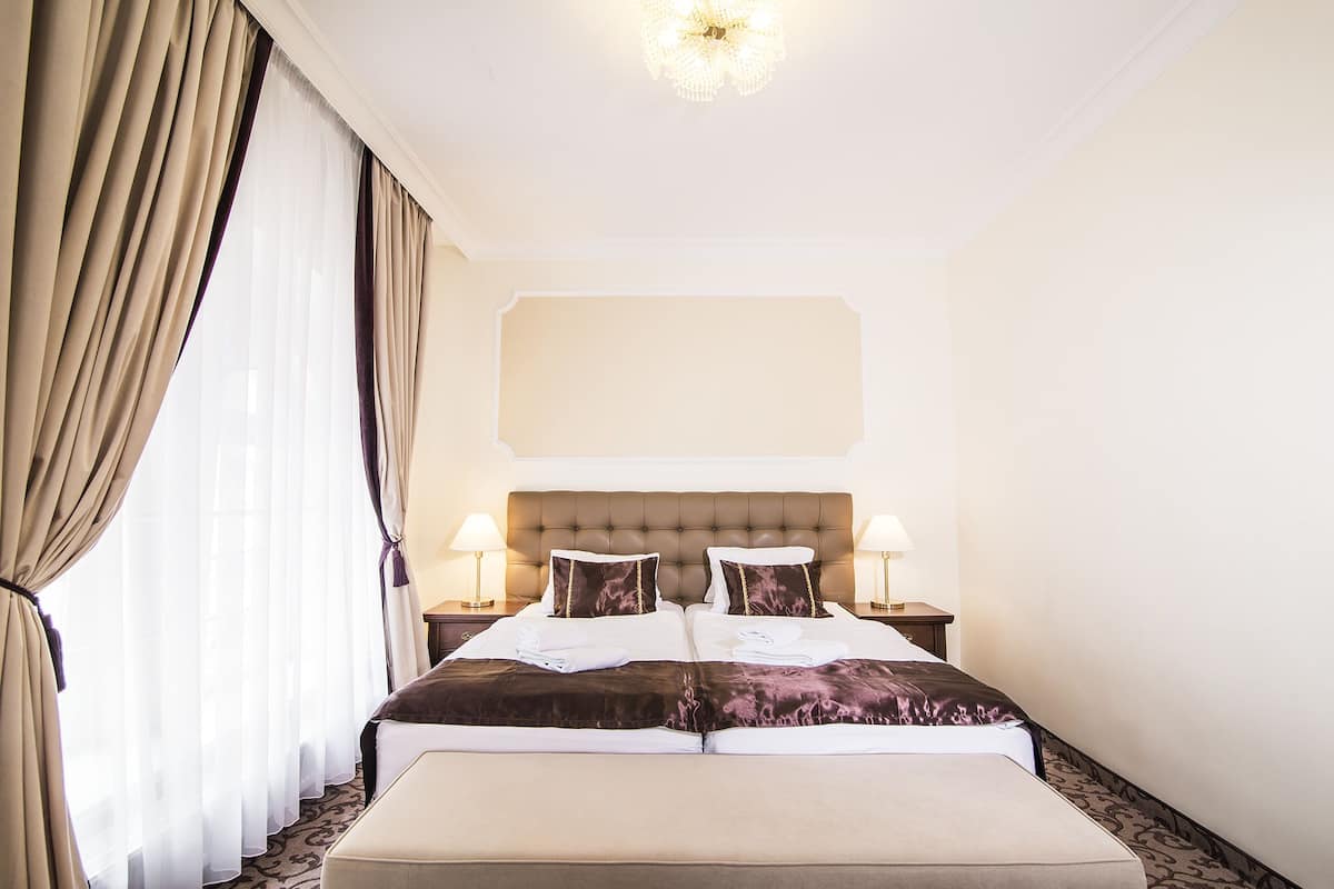 Quarto de hotel com uma cama grande, duas mesas de cabeceira com abajures e um candelabro.