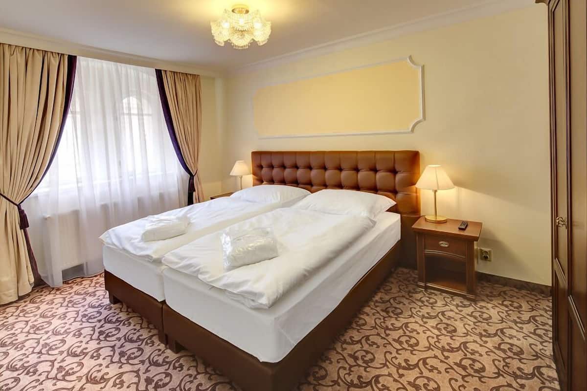 Quarto de hotel com uma cama de casal, duas mesas de cabeceira com abajures, um espelho grande acima da cama e um tapete estampado.