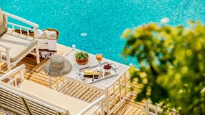 Uma área à beira da piscina com uma mesa posta para refeições e bebidas, cercada por espreguiçadeiras e um deck de madeira.